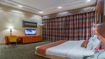 Quarto de hotel com uma cama, uma escrivaninha com cadeira, televisão e telefone.