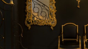 Um quarto com um espelho grande e decorativo, um candelabro e duas cadeiras.