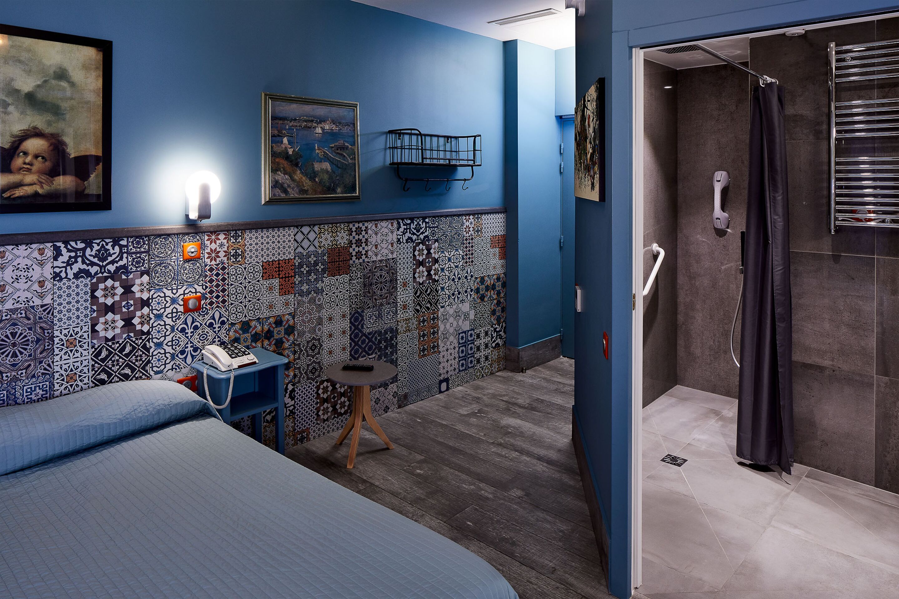 Quarto com cama, uma mesinha com telefone, parede com azulejos estampados e área de chuveiro.