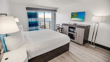 Quarto de hotel com cama, escrivaninha, televisão e varanda com vista para o mar.