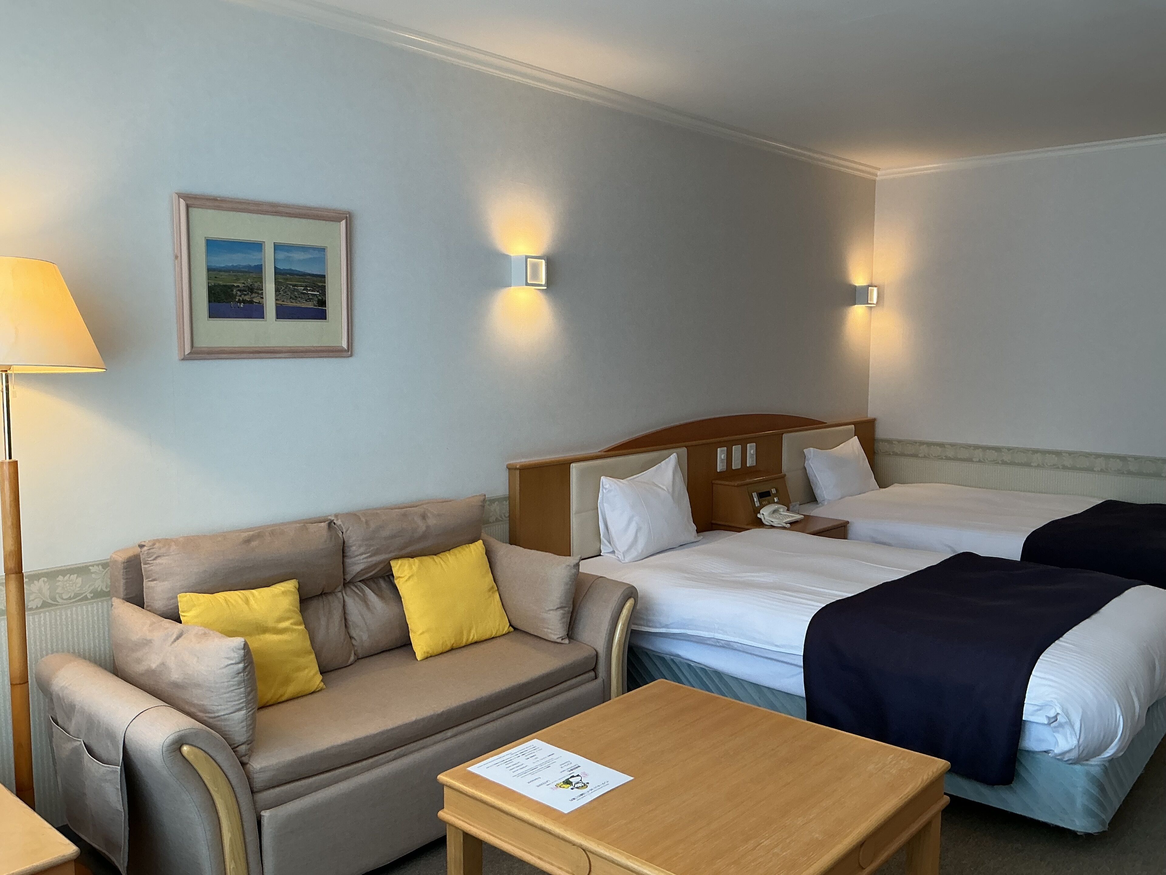Quarto de hotel com sofá, duas camas, uma mesa de madeira e um quadro na parede.