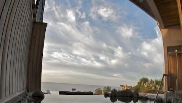 Visão nítida de uma piscina com uma parede de pedra de um lado e uma estrutura de madeira do outro, refletindo o céu e as nuvens.