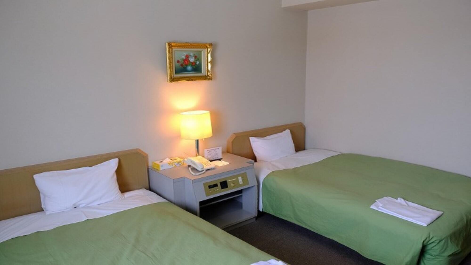 Quarto de hotel com duas camas, uma mesa de cabeceira com abajur, telefone e um quadro na parede.