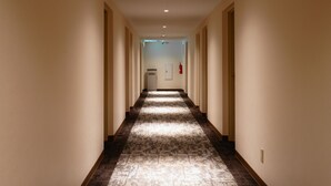 Um corredor comprido e estreito, com piso coberto de carpete e paredes bege.