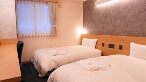 Quarto de hotel com duas camas, uma escrivaninha e uma janela com cortinas.
