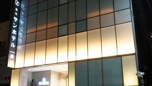 Entrada de hotel com uma escadaria que leva ao interior, uma máquina de vendas automática e uma placa com caracteres japoneses.