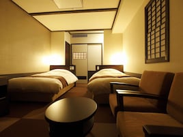 Quarto de hotel com duas camas de solteiro, um sofá, uma mesinha e vista para o corredor.