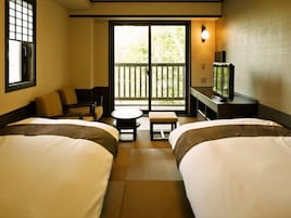 Quarto de hotel com duas camas, uma mesinha, uma cadeira, televisão e varanda com vista para o verde.