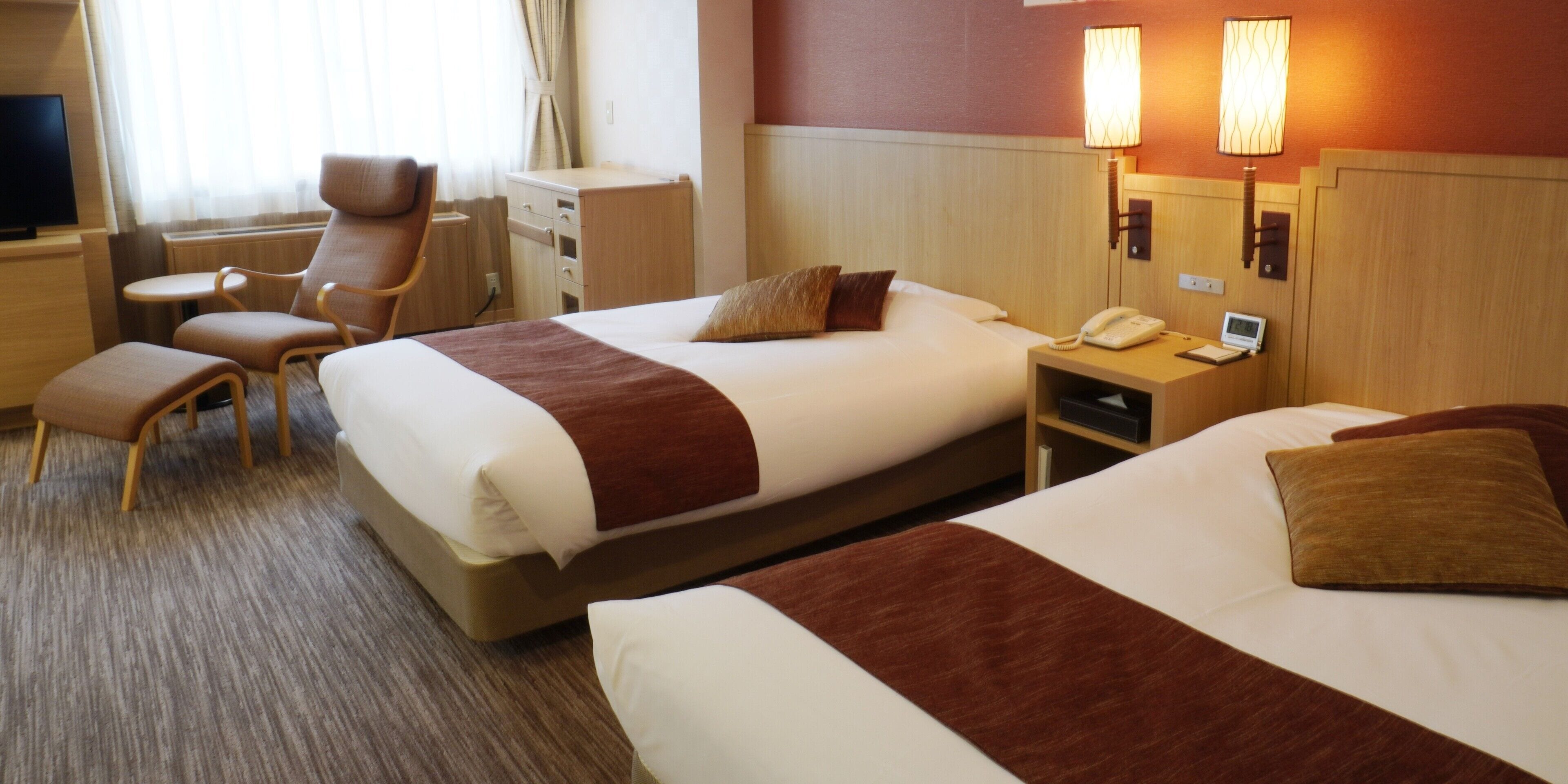 Quarto de hotel com duas camas, uma escrivaninha com cadeira, televisão e uma luminária.