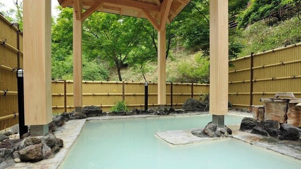 Uma onsen japonesa tradicional com estrutura de madeira, cerca de bambu e piscina revestida em pedra.