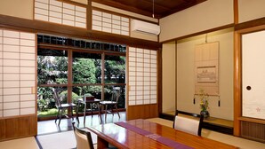 Um quarto japonês tradicional com tatames, uma mesa de madeira e vista para um jardim através de amplas janelas.