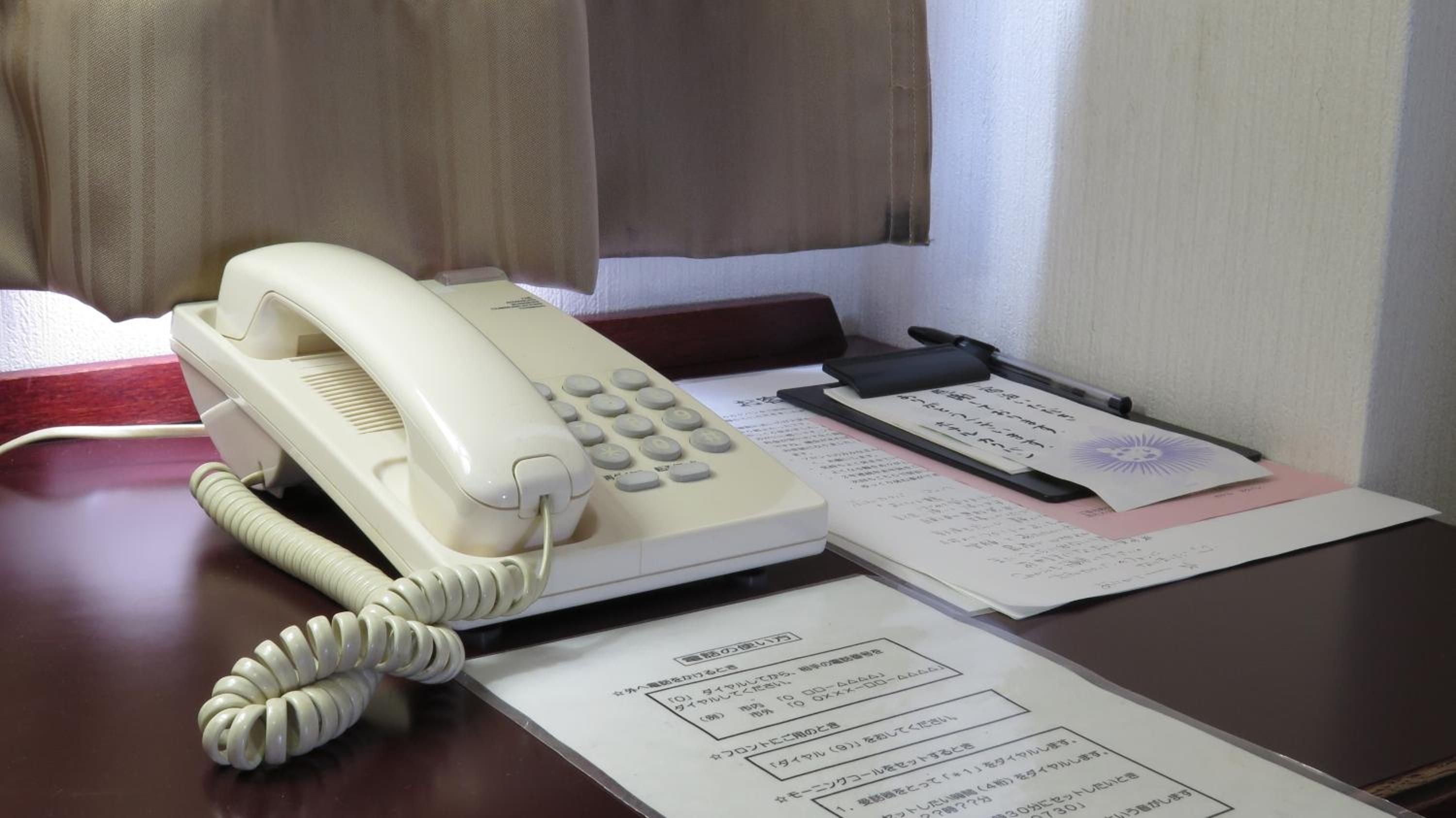 Quarto de hotel com telefone, bloco de notas e caneta na mesa.