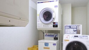 Uma lavanderia com duas máquinas de lavar, um secador e uma pequena cesta amarela.