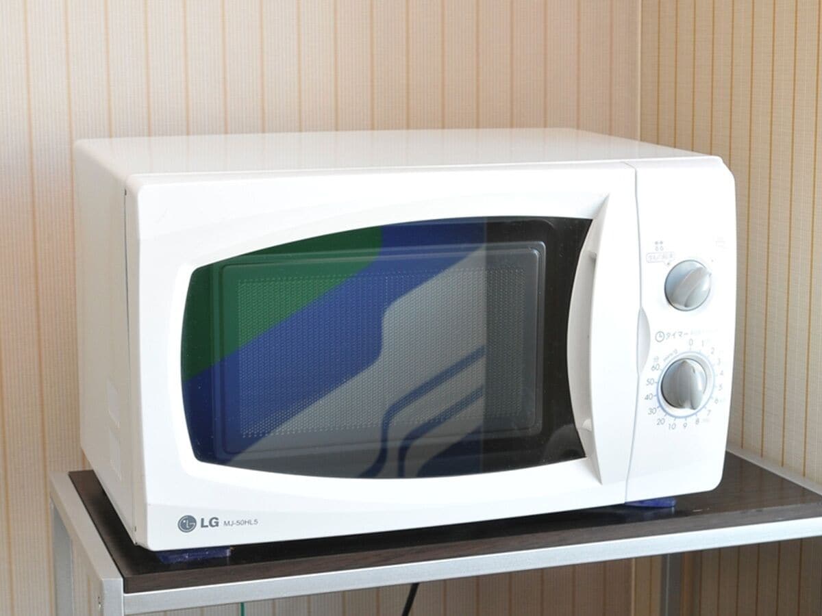 Um forno de micro-ondas branco com visor digital e duas manivelas sobre uma superfície metálica.