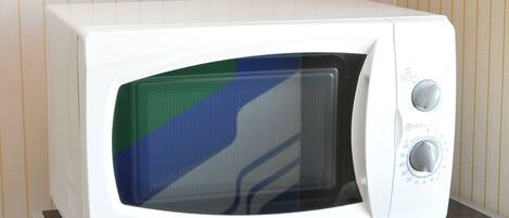 Um forno de micro-ondas branco com visor digital e duas manivelas sobre uma superfície metálica.