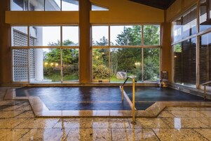 Piscina ampla em ambiente interno, com paredes de vidro transparente e vista para o exterior.