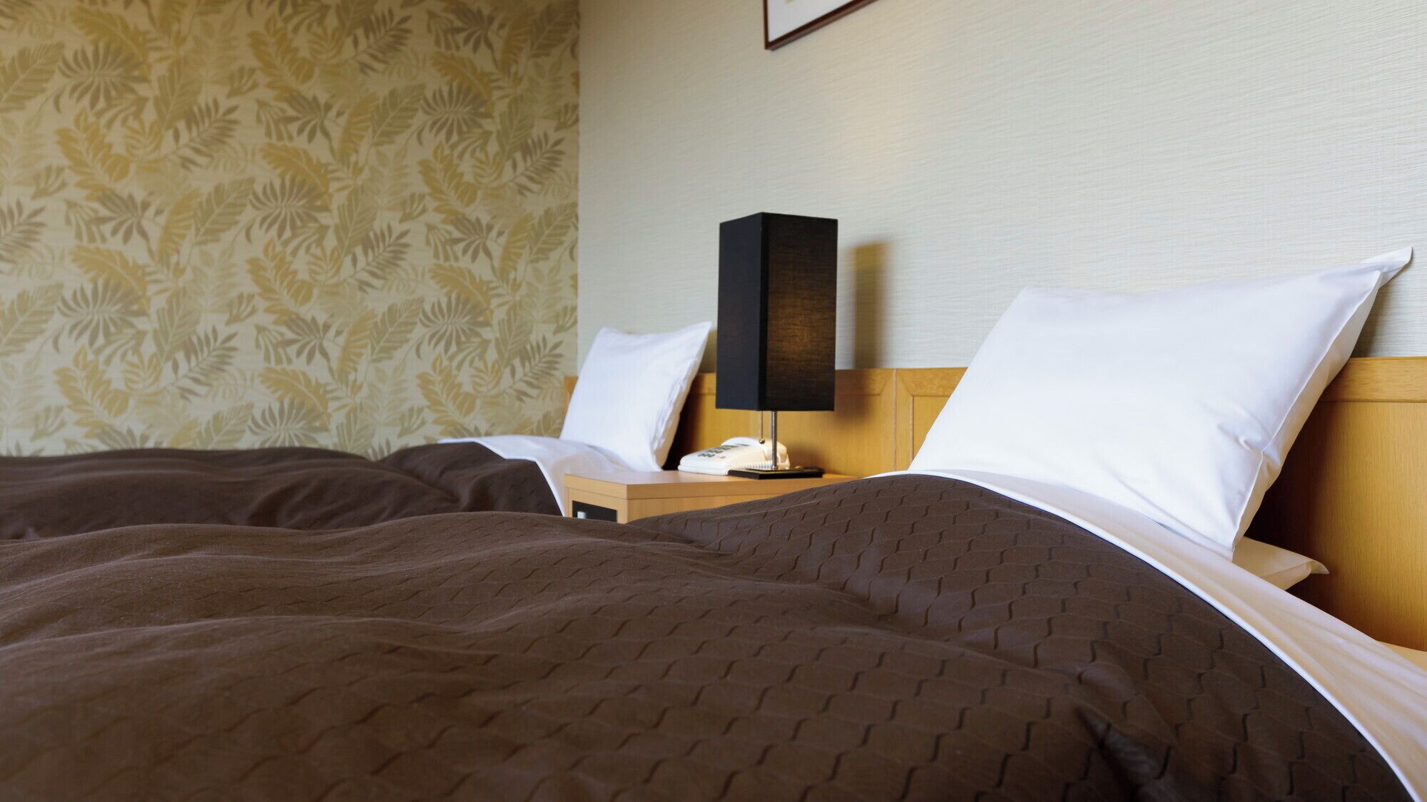 Quarto de hotel com cama, mesa de cabeceira, abajur e telefone.