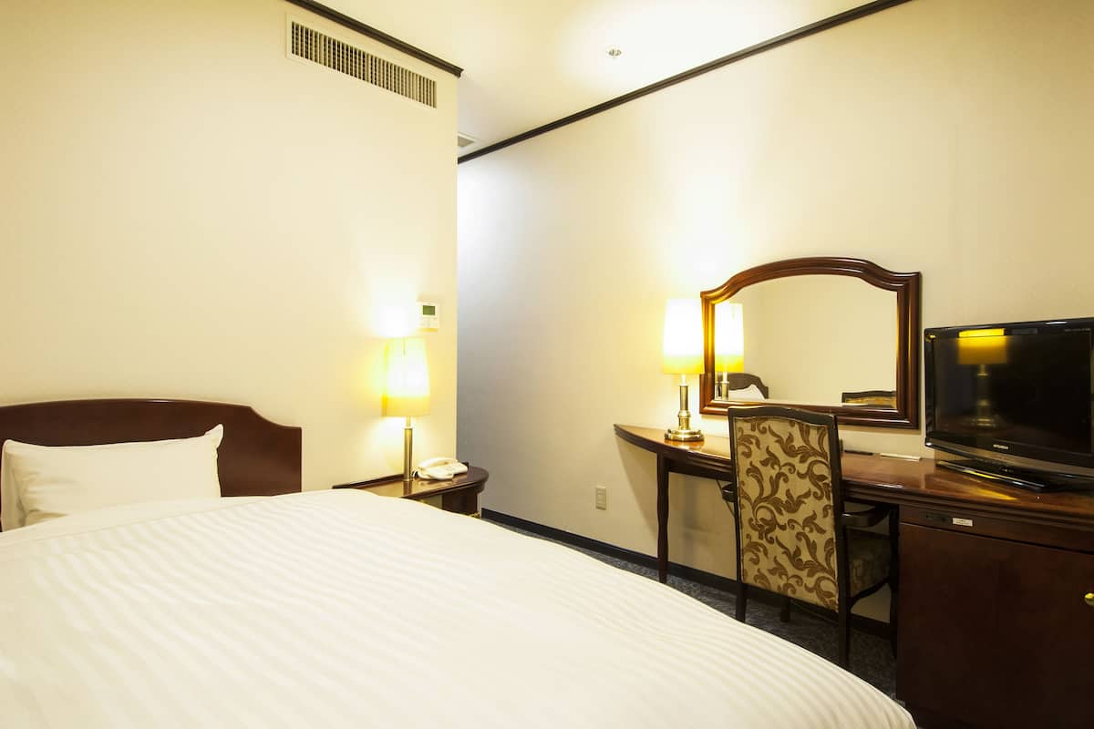 Quarto de hotel com uma cama grande, luminárias laterais, uma escrivaninha com espelho e uma televisão.