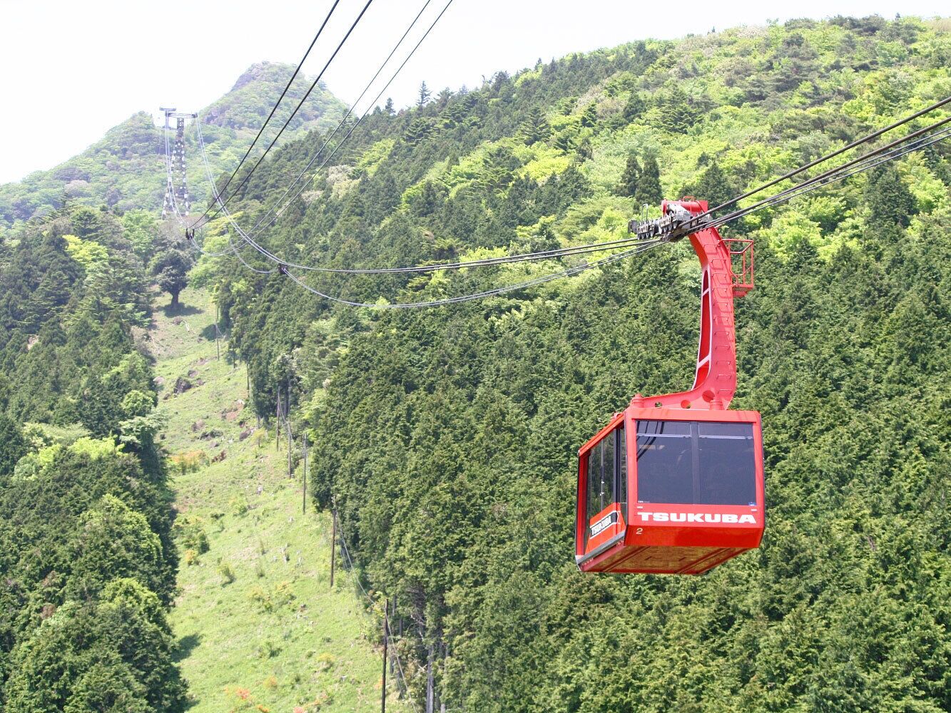 Um teleférico vermelho suspenso sobre uma montanha verdejante e florestada.