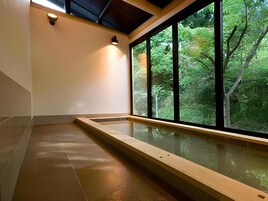 Uma área de spa com um banco de madeira, um compartimento envidraçado e vista para uma floresta através de grandes janelas.