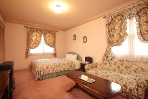 Quarto com duas camas, um sofá, uma mesa de madeira e uma escrivaninha.