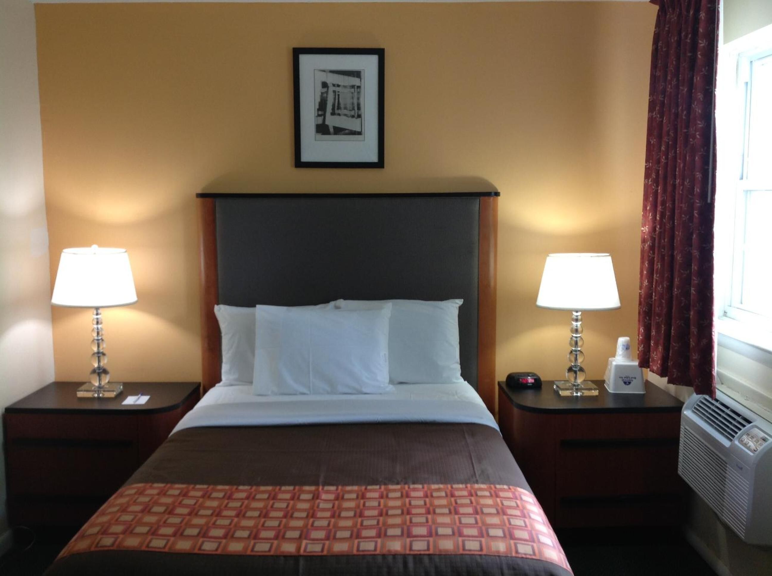 Quarto de hotel com uma cama, duas mesas de cabeceira, um quadro na parede e uma janela com cortinas.