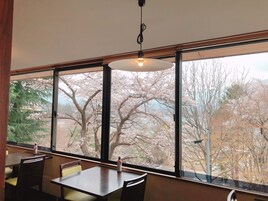 Uma área de refeições com mesa e cadeiras, um lustre pendurado e uma grande janela com vista para cerejeiras em flor.