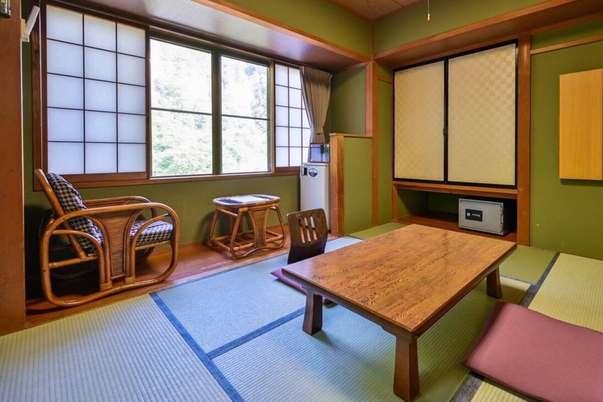Um quarto japonês tradicional com piso de tatame, uma mesa de madeira baixa e uma área de estar com mesa e cadeiras de madeira.