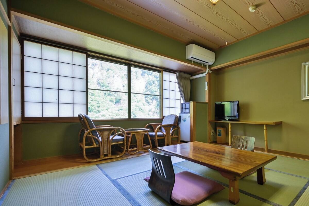 Um quarto japonês tradicional com tatames, uma mesa baixa e uma televisão em uma prateleira.