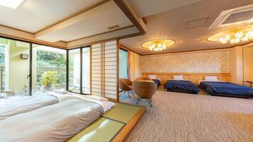 Quarto de hotel com cama, duas mesas de cabeceira, uma cadeira, um sofá e vista para área verde pelas janelas.