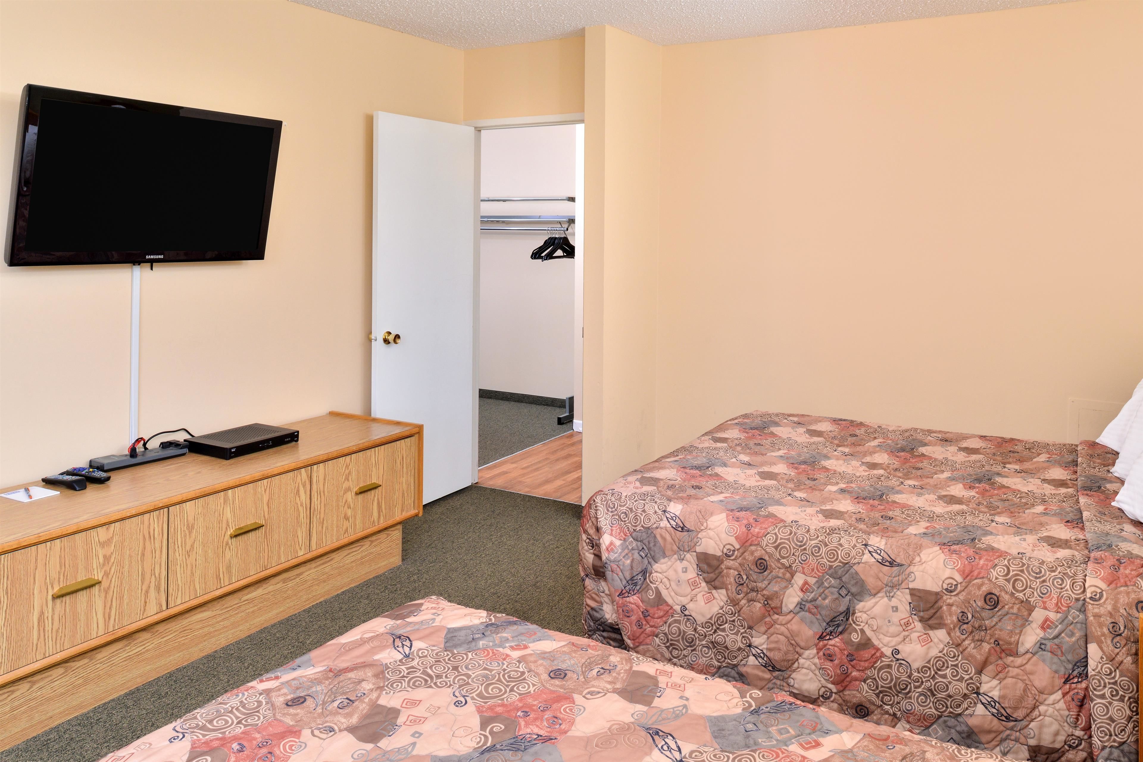 Quarto de hotel com uma cama, televisão fixada na parede, cómoda de madeira e roupeiro com cabides.