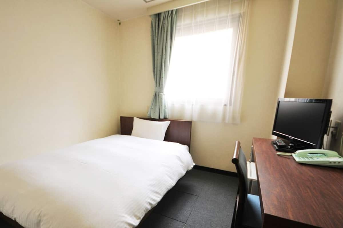 Quarto de hotel com uma cama, uma mesa de trabalho e uma janela com cortinas.