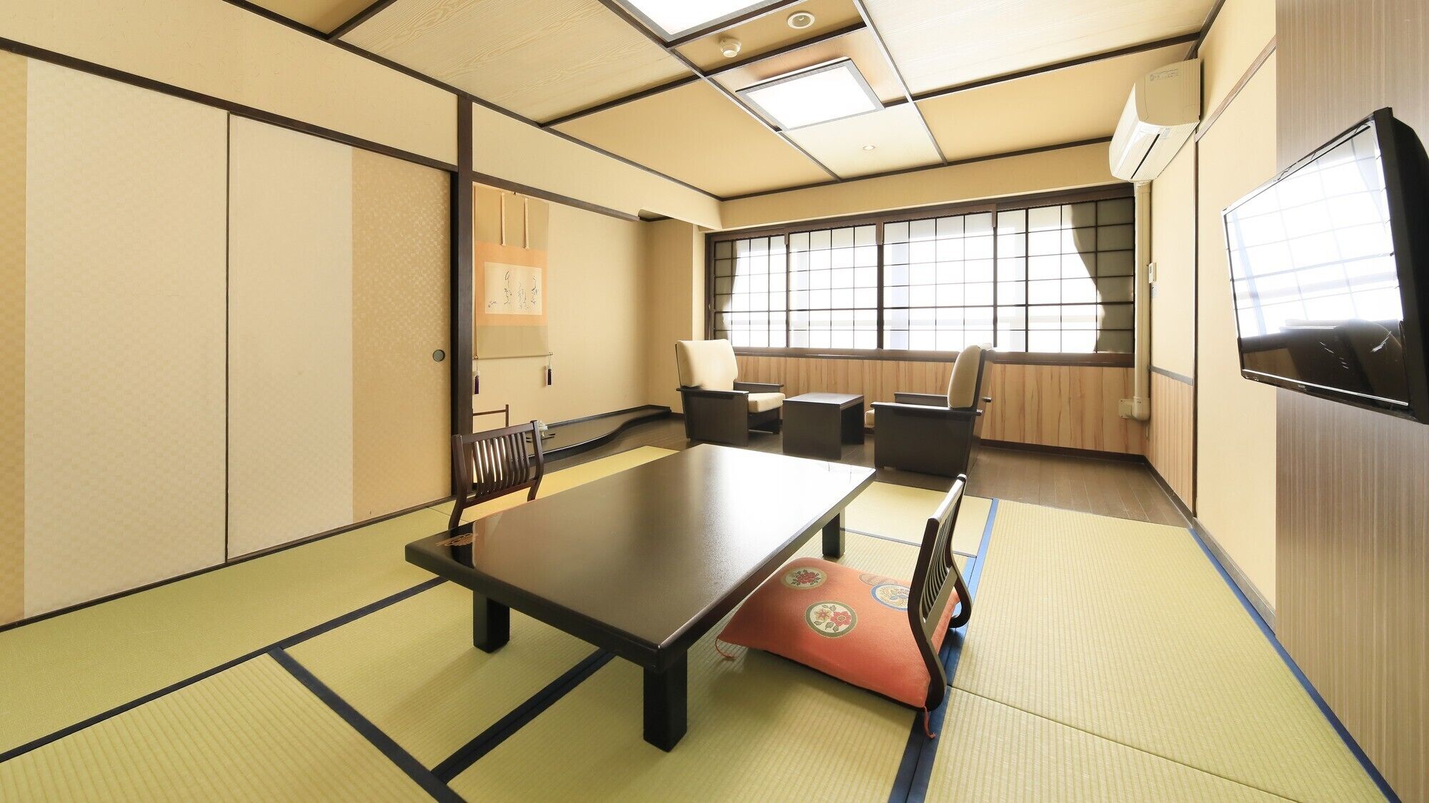 Um quarto tradicional japonês com tatames, uma mesa baixa, cadeiras e uma janela grande.