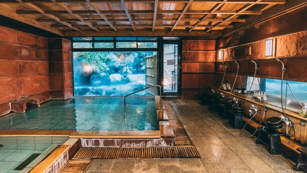 Uma onsen japonesa tradicional com interior de madeira, uma banheira de águas termais e uma fileira de lavatórios.