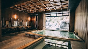 Uma onsen japonesa tradicional com interiores de madeira, uma nascente termal e vista para uma cascata.