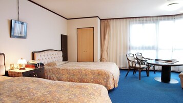 Quarto de hotel com duas camas, uma escrivaninha, cadeiras, um abajur e um guarda-roupa.