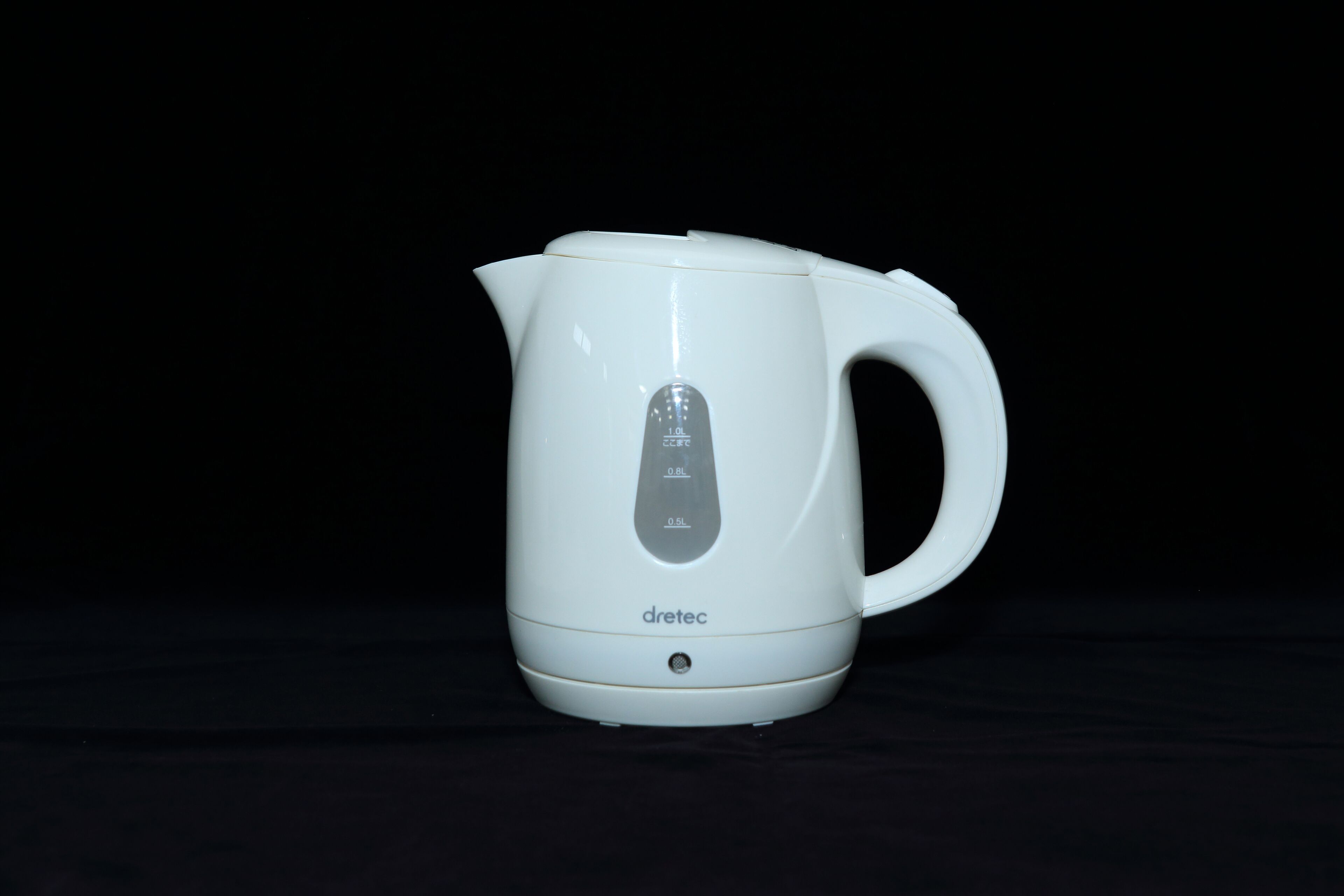 Uma chaleira elétrica branca com visor digital e um puxador, apoiada em uma superfície escura.