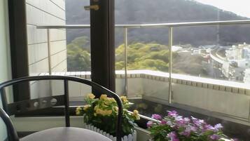 Varanda com cadeira e plantas em vasos, com vista para um horizonte urbano com edifícios e áreas verdes.