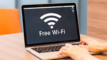 Um laptop sobre uma mesa de madeira, com a tela exibindo 'Free Wi-Fi'.
