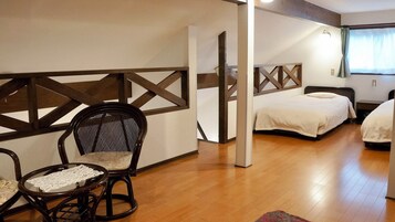 Um quarto com piso de madeira, duas camas, uma cadeira e uma mesa.