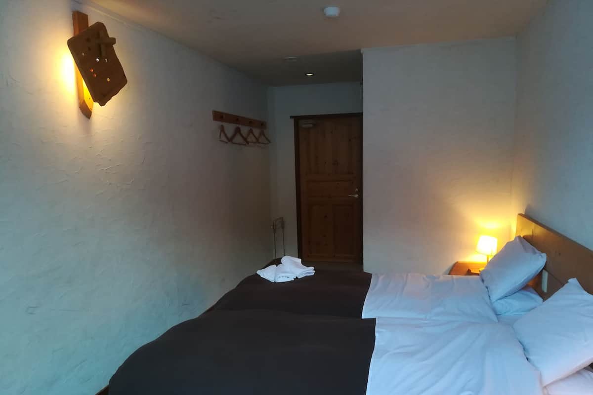 Quarto de hotel com cama, porta de madeira e luminária fixada na parede.