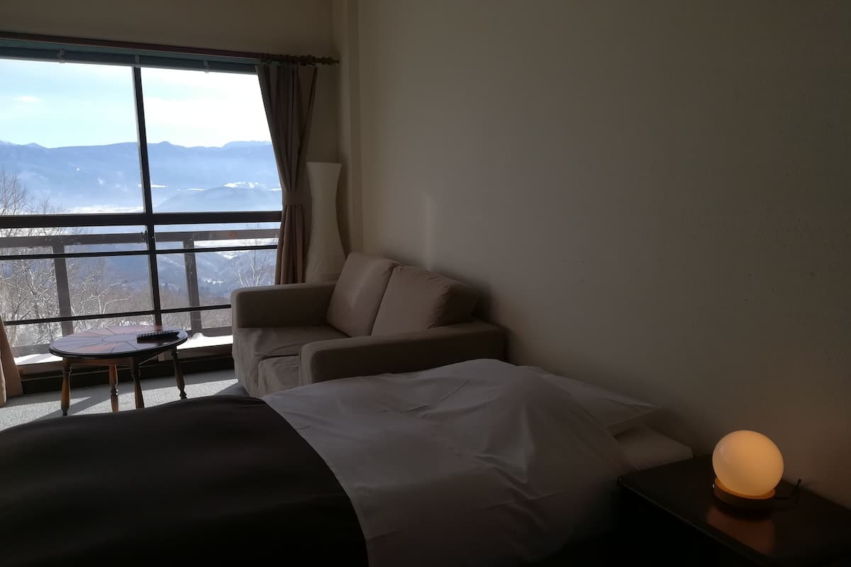 Quarto de hotel com uma cama, um sofá, uma mesinha e uma luminária.