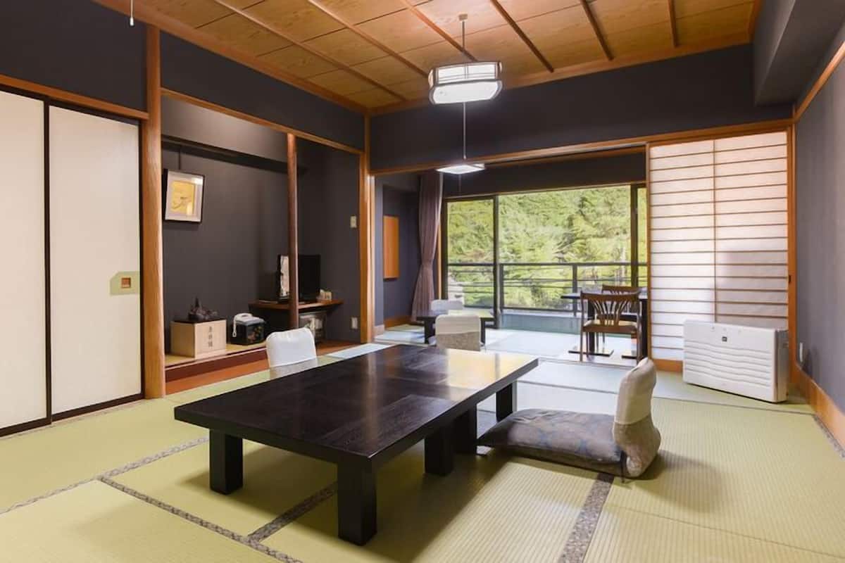 Um quarto japonês tradicional com tatames, uma mesa baixa, uma poltrona acolchoada, portas deslizantes e vista para o verde.