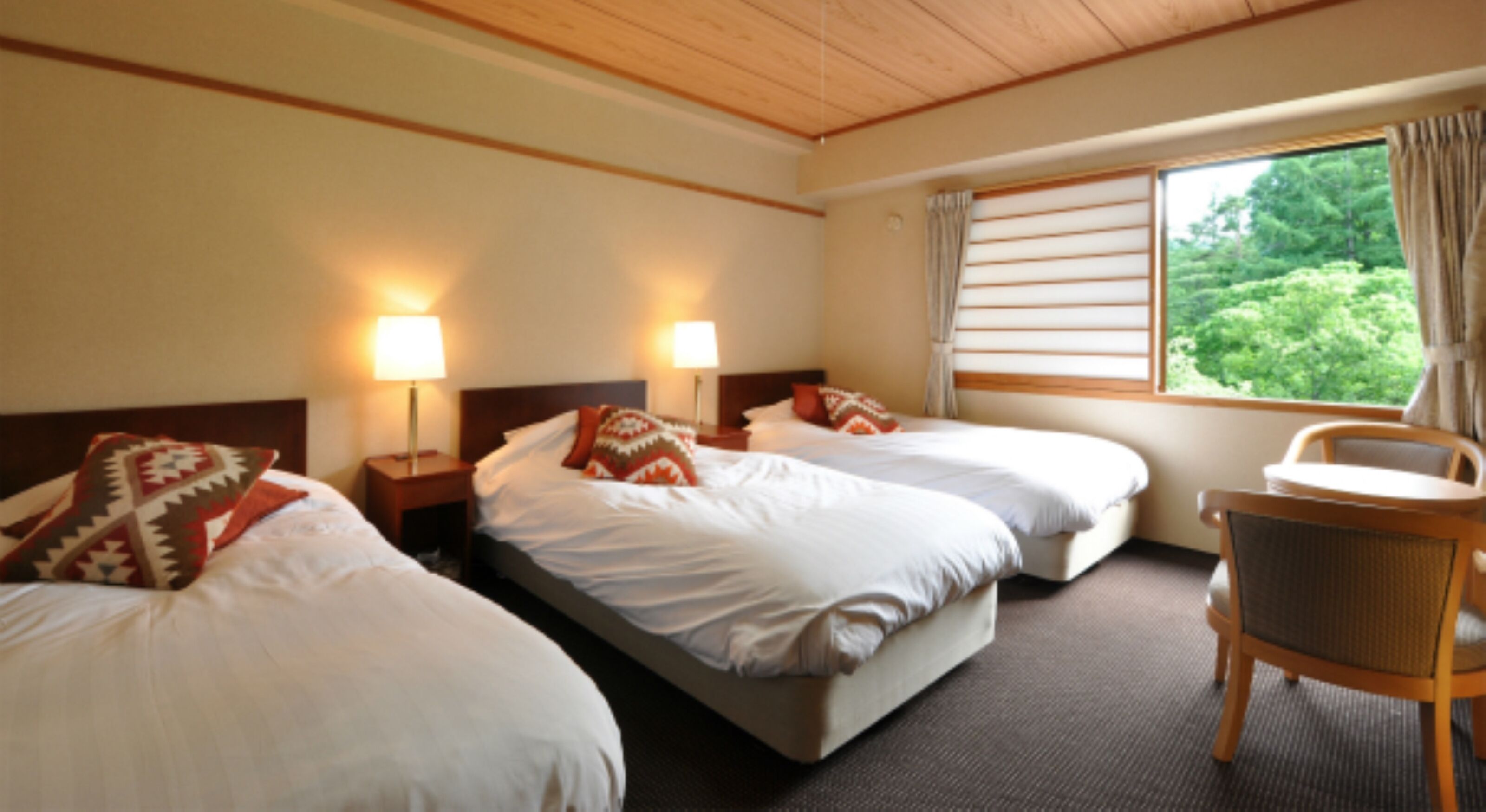 Quarto de hotel com duas camas, uma cadeira e uma janela com persianas.