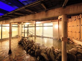 Uma onsen japonesa tradicional com degraus de pedra que levam a uma nascente termal, rodeada por paredes de madeira e um chão ladrilhado.