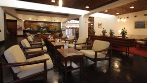 Um hall amplo com mobiliário de madeira, área de cozinha ao fundo e plantas em vasos.