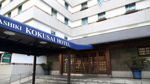 A entrada do Hotel Ashiki Kokusai com uma escadaria coberta e plantas em vasos.