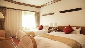 Quarto de hotel com duas camas, uma escrivaninha, uma cadeira e um abajur.