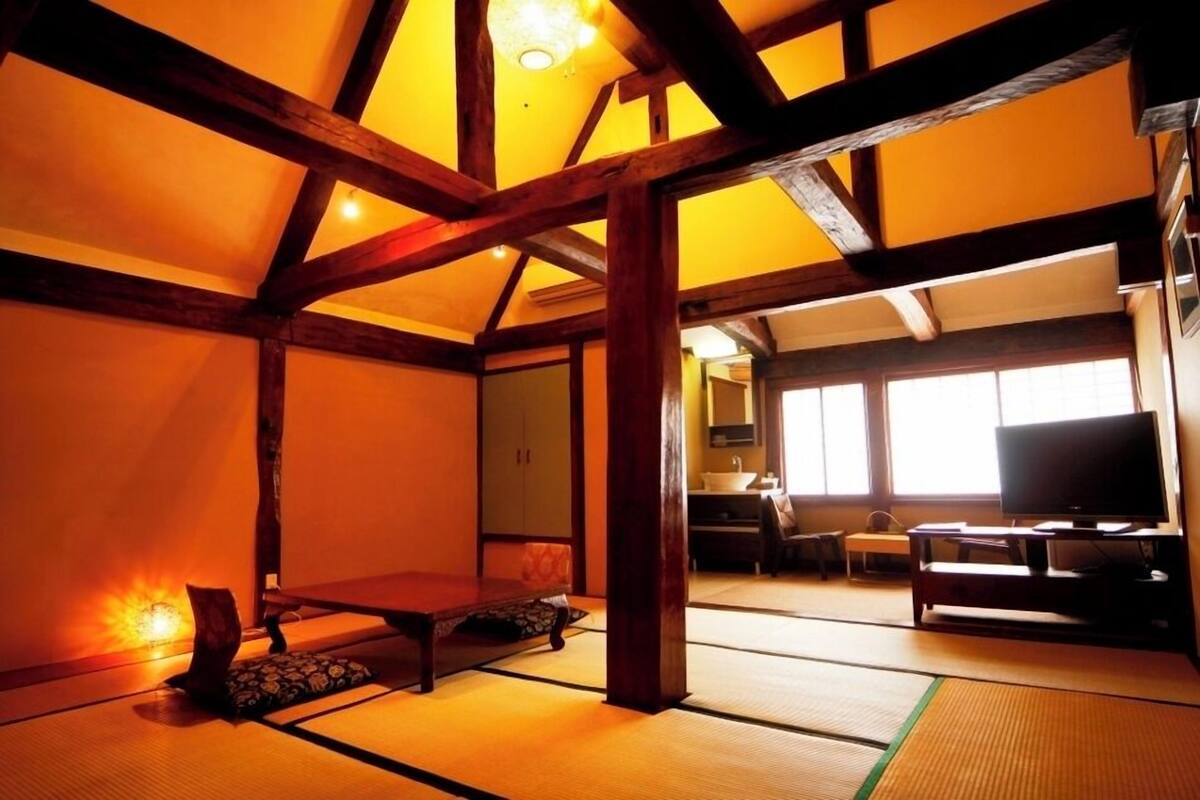 Um quarto japonês tradicional com tatames, uma mesa baixa e uma televisão.