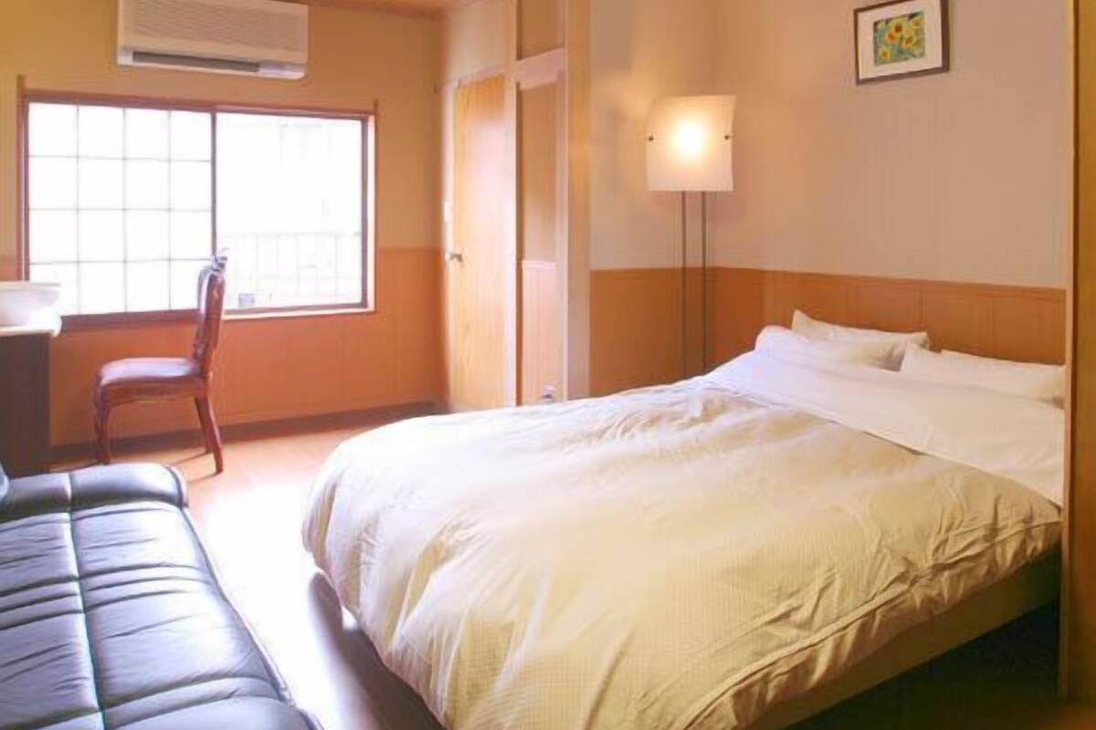 Quarto de hotel com cama, poltrona, escrivaninha e janela.